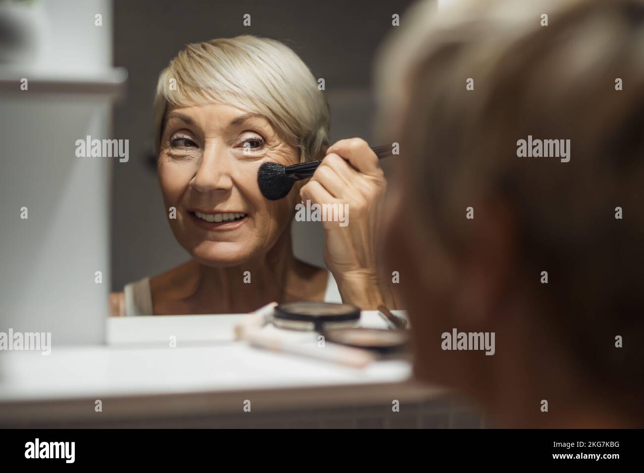 Mature woman is applying blush in the bathroom Stock Photo - Alamy