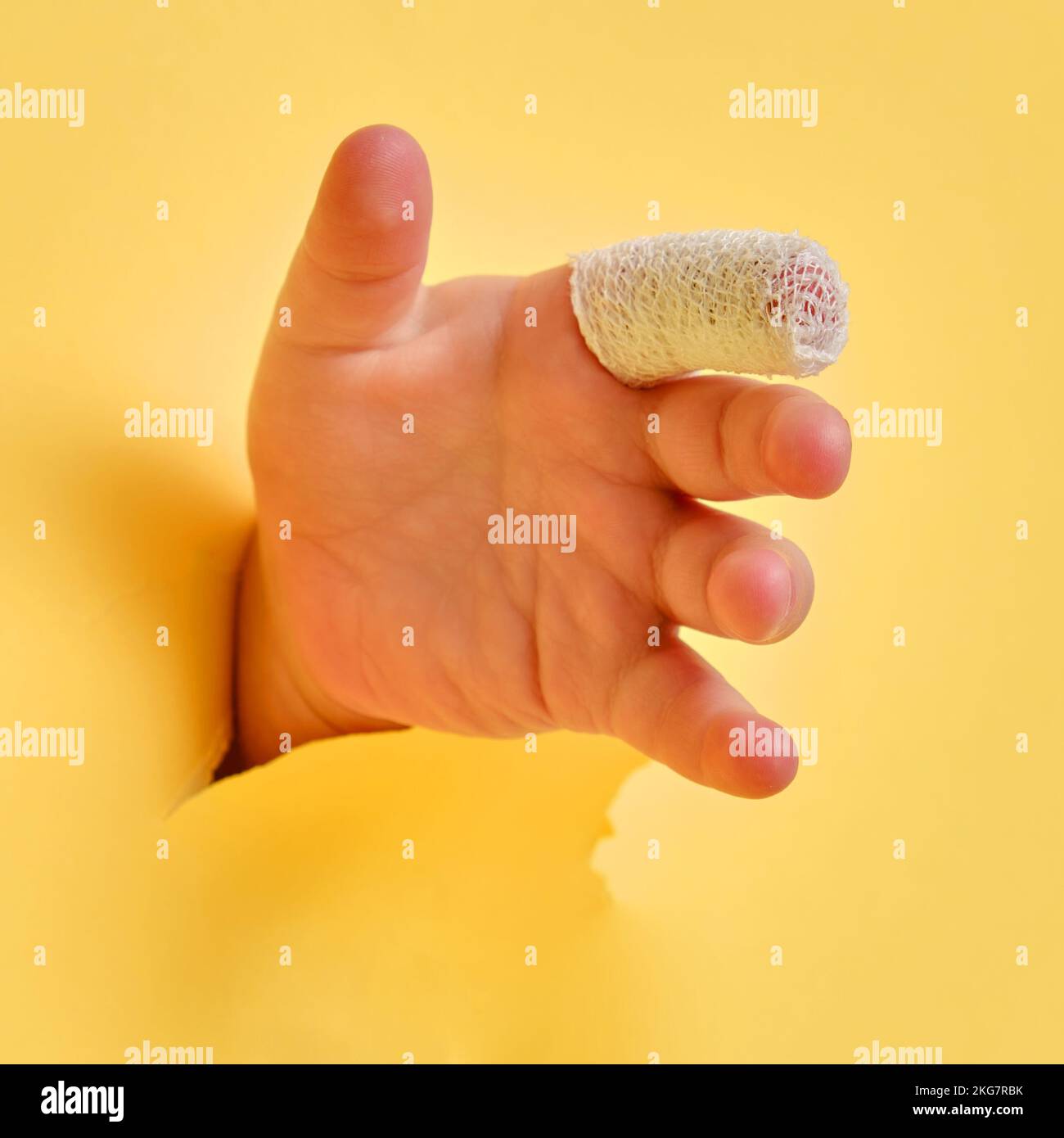 Baby s hand with a bandaged finger on a yellow studio background, close ...