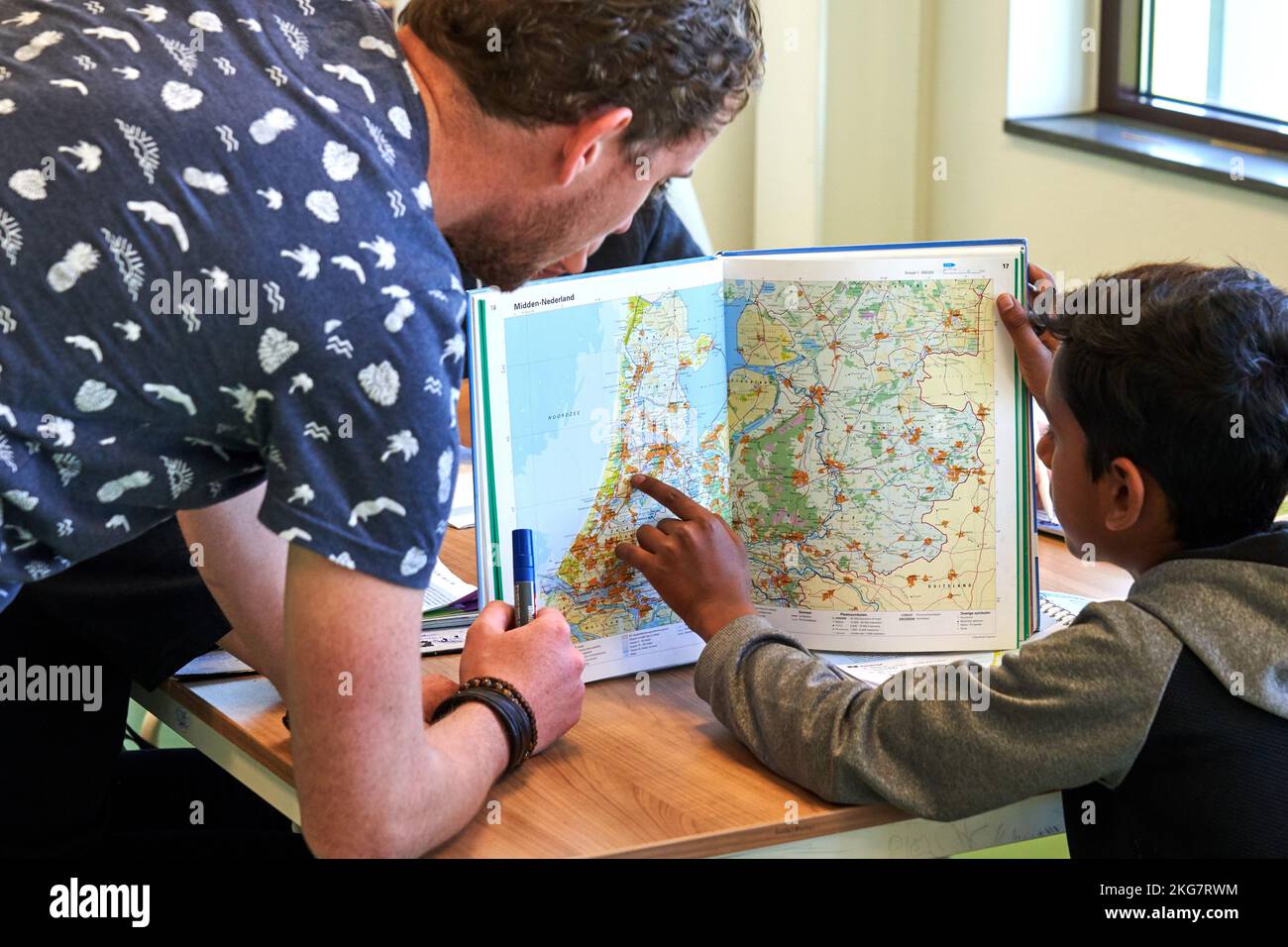 Teacher with students with a geography book in a classroom in a ...