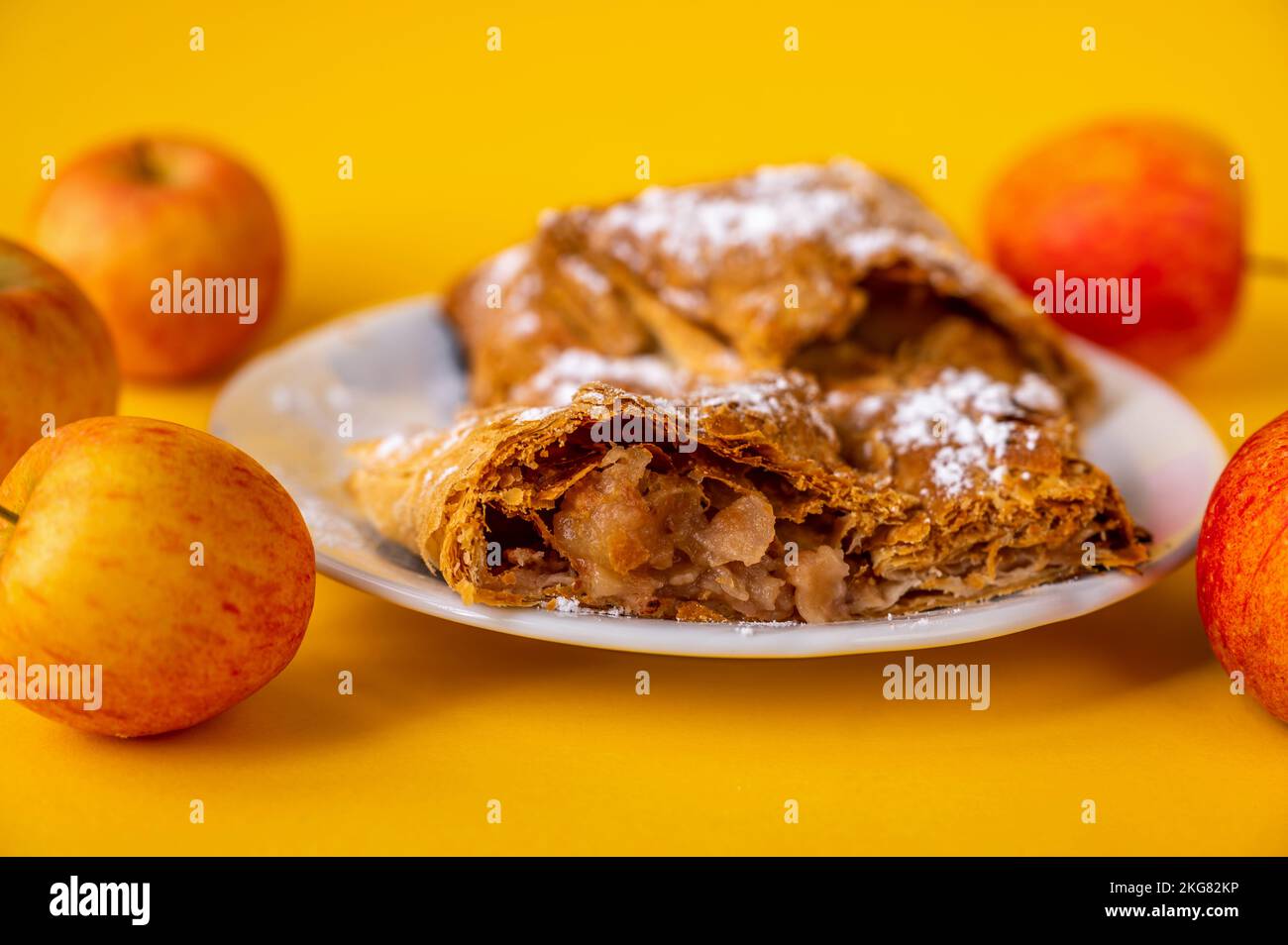 Two piece of apple pie (strudel) on white plate, 5 apple on yellow ...