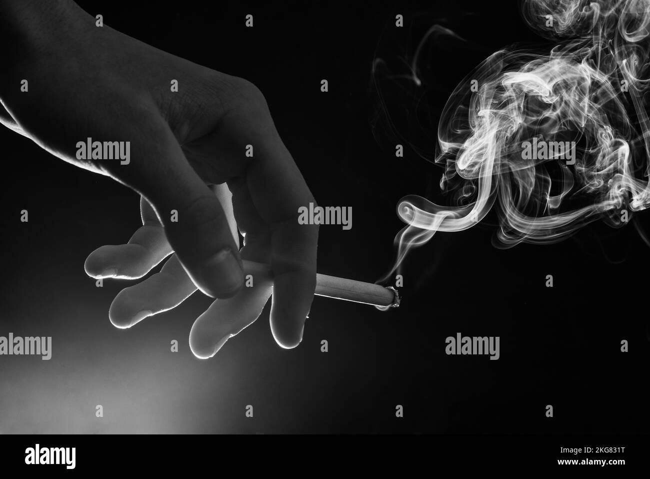 Male hand hold burning cigarette with swirl of smoke dark background ...