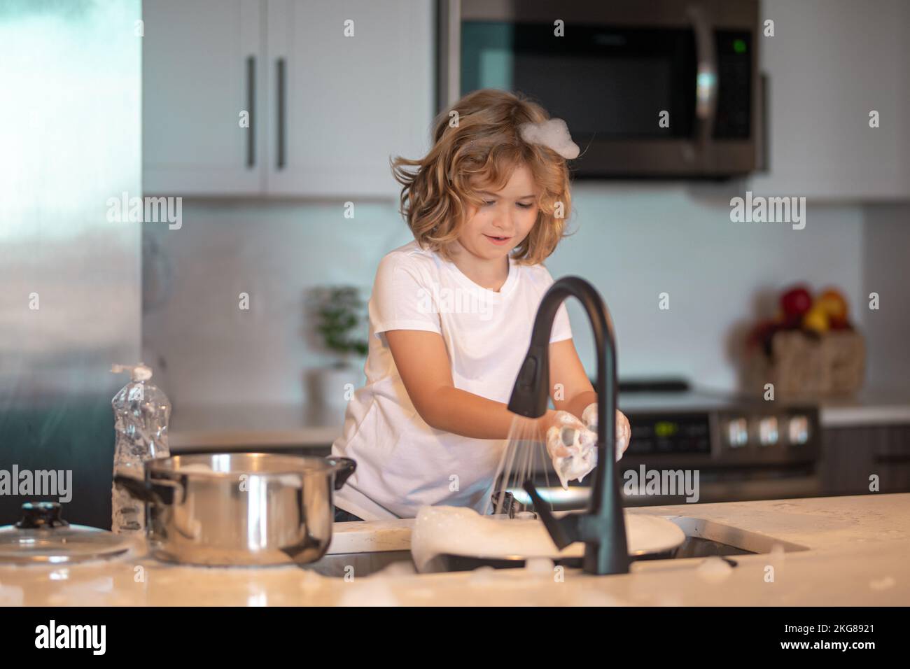 Funny twin boys helping in kitchen with washing dishes. Children having fun with housework. A ...