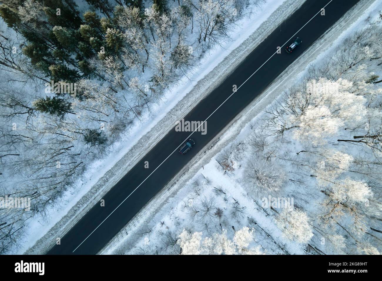 Aerial view of winter landscape with snow covered woods and black asphalt forest road on cold ...