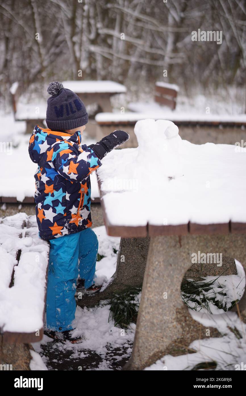 A cute Caucasian kid playing with the snow in the park in winter Stock ...