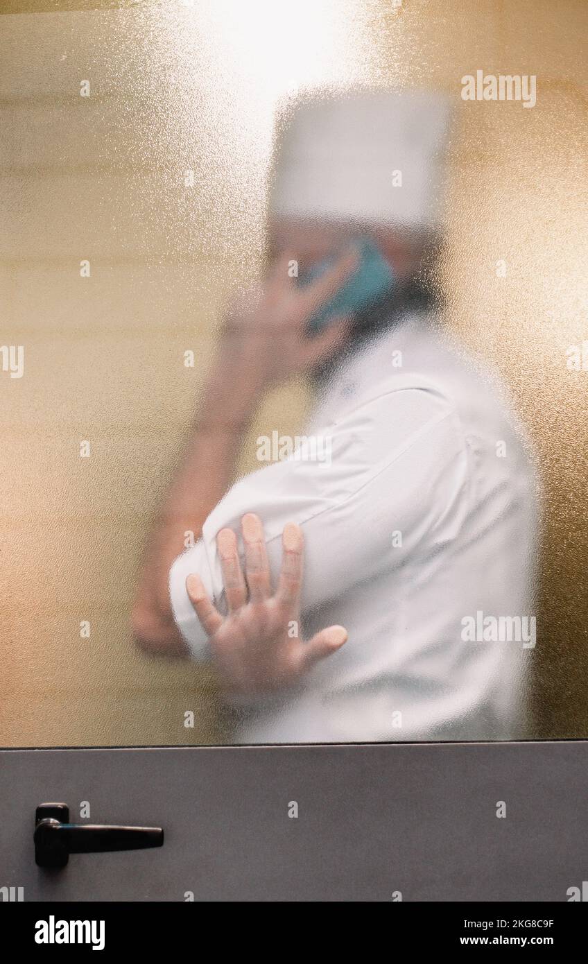 silhouette behind the glass of a man in a chef's uniform talking on the ...
