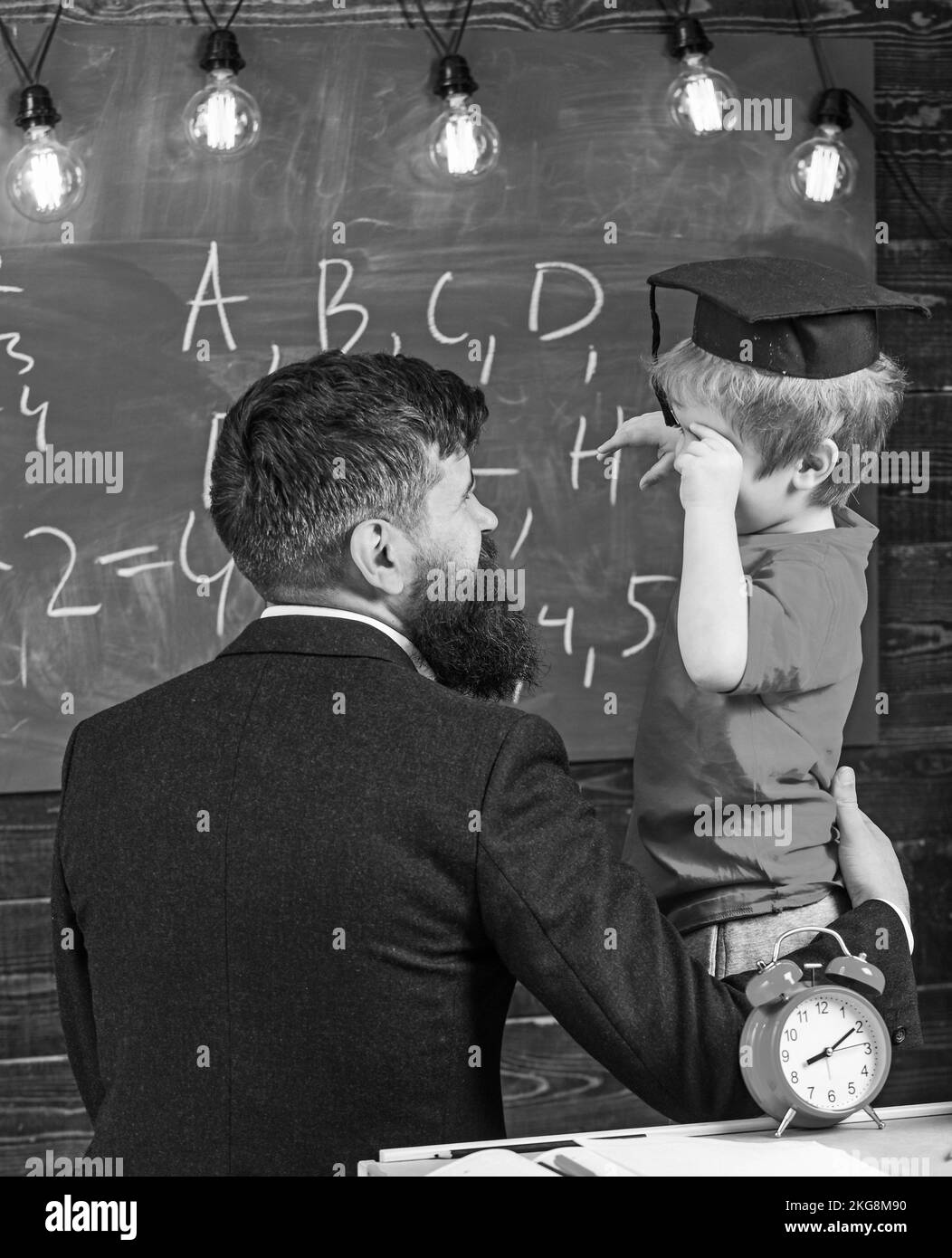 Boy, child in graduate cap discussing scribbles on chalkboard while ...