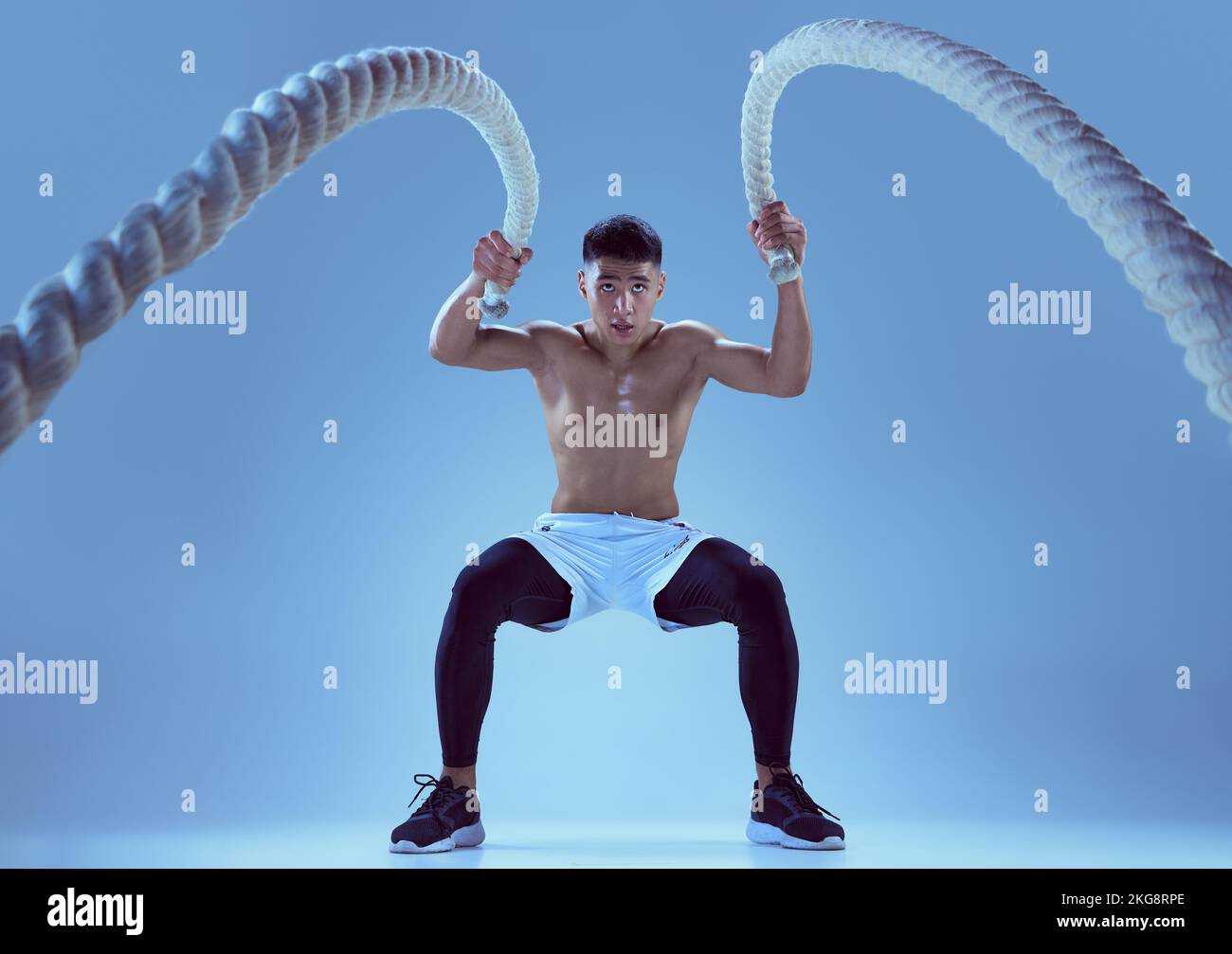 Portrait of young muscular man training, pulling rope isolated over ...