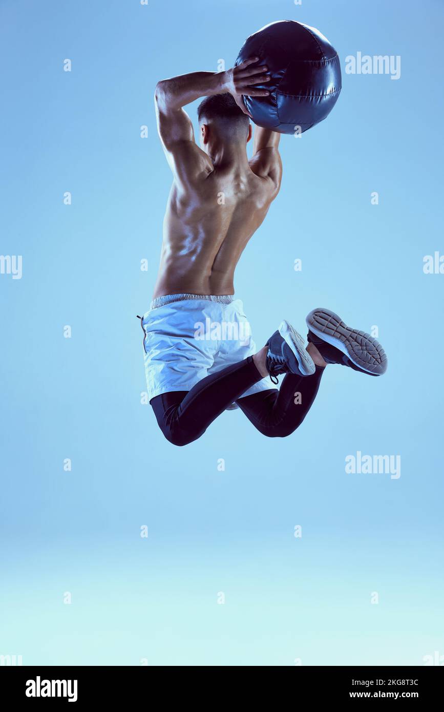 Portrait of young muscular man training, throwing med ball in a jump ...