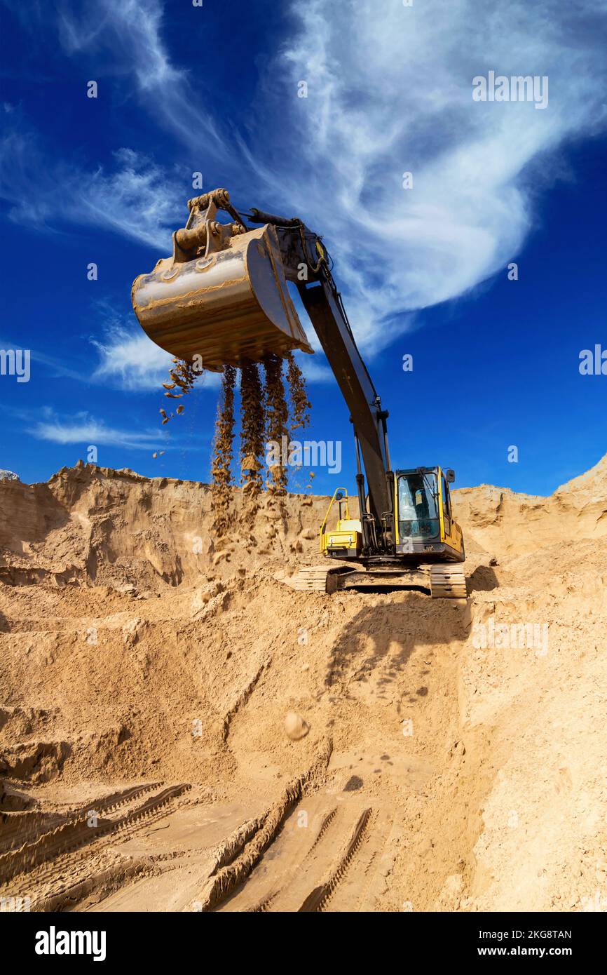 Yellow excavator working with sand at construction site in sunny day ...