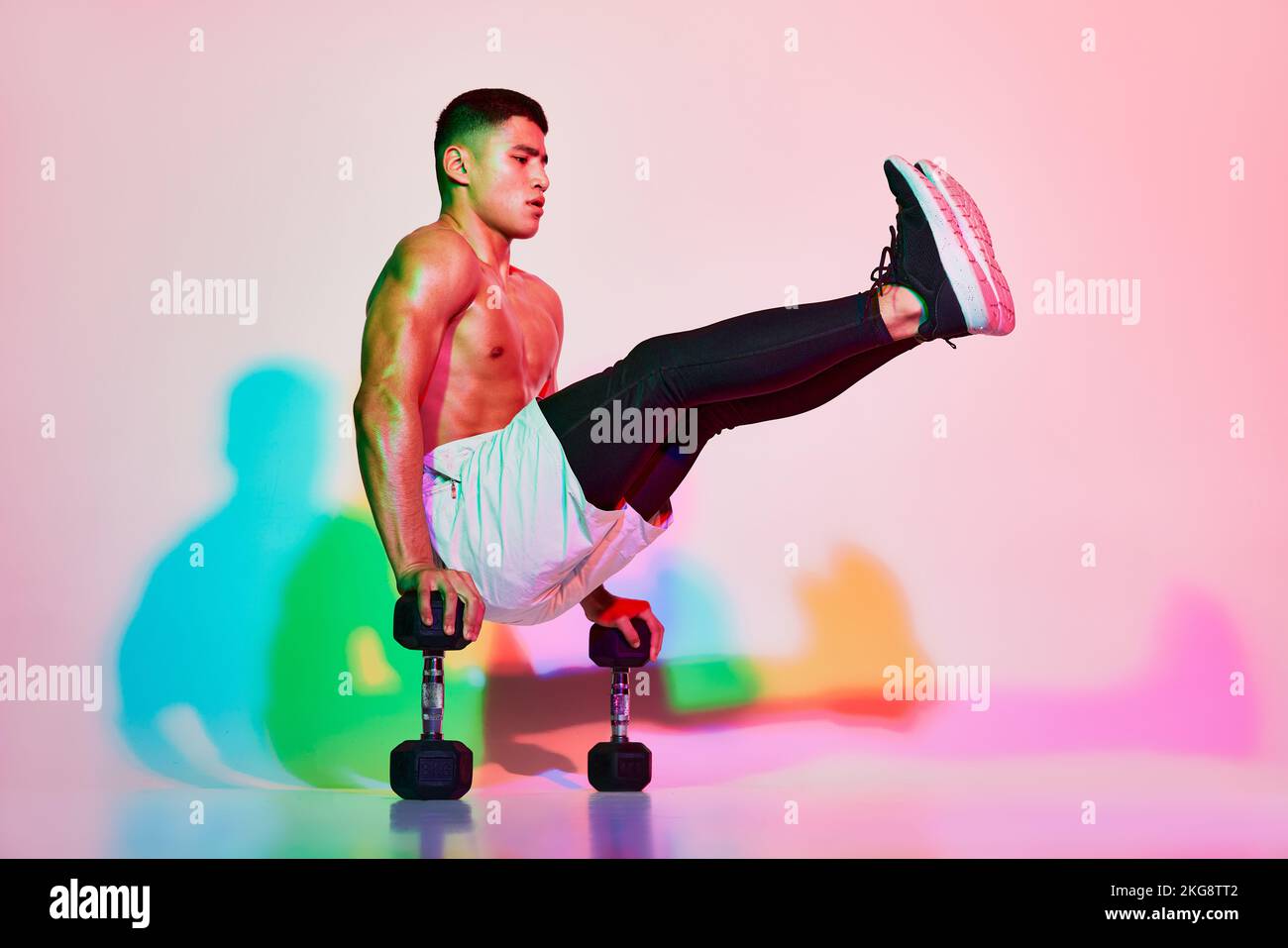 Portrait of young muscular man training, standing on dumbbells and ...