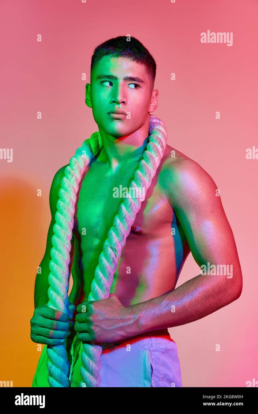 Portrait of young muscular man training, posing with rope isolated over ...
