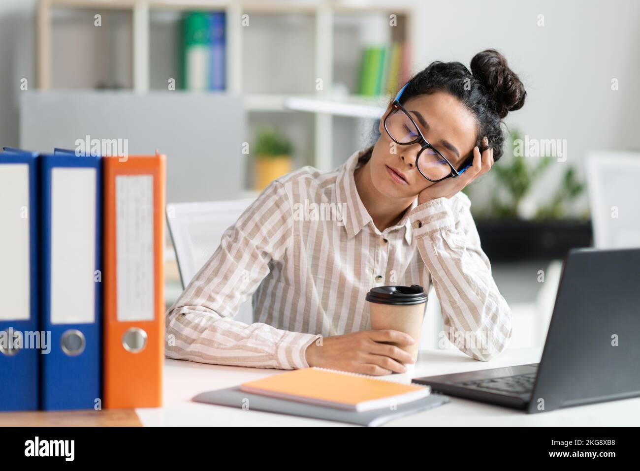 Tired female employee sleeping at work, exhausted woman resting at desk near laptop and folders ...