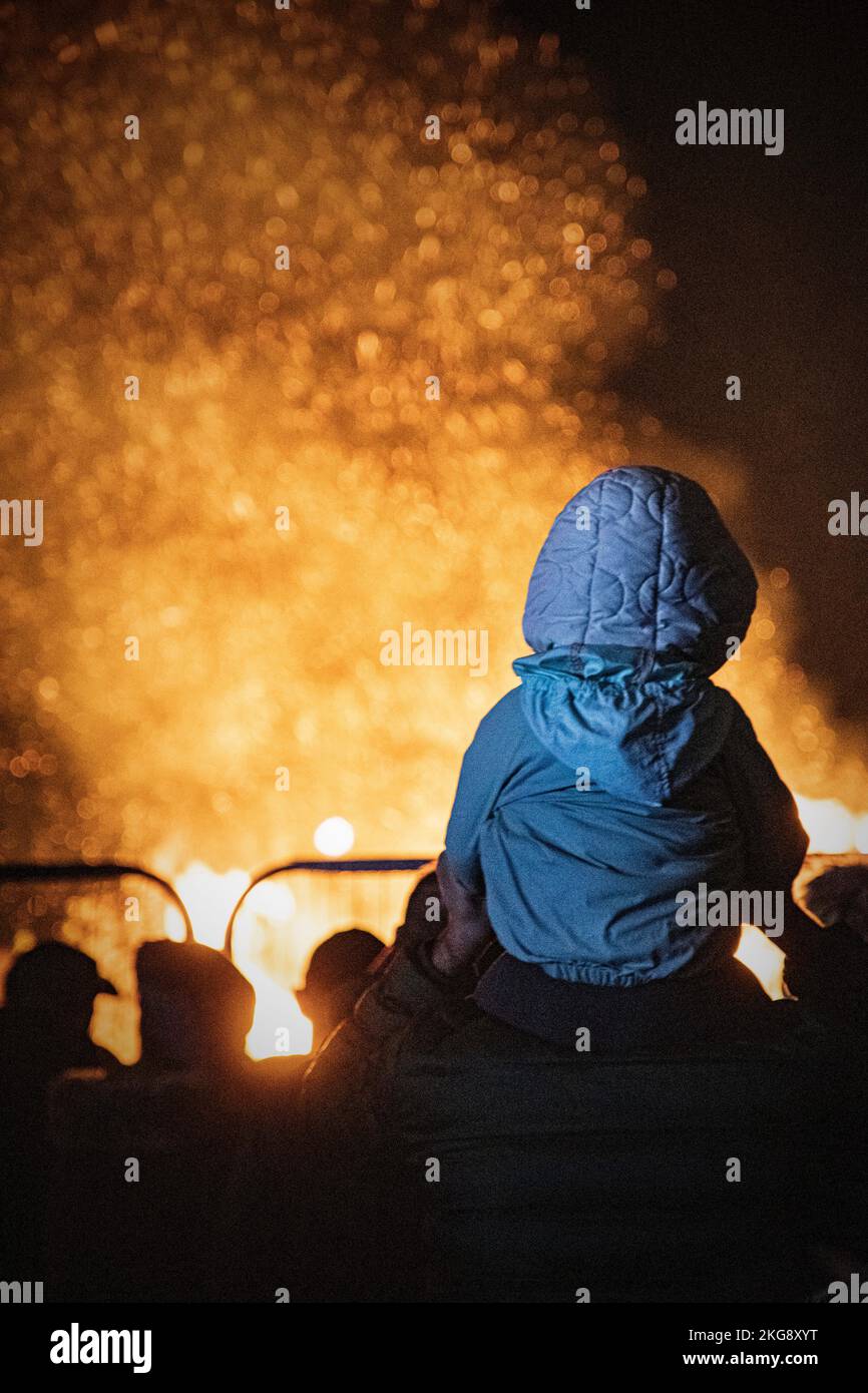 Children on their parents shoulders stood in front of a roaring bonfire ...