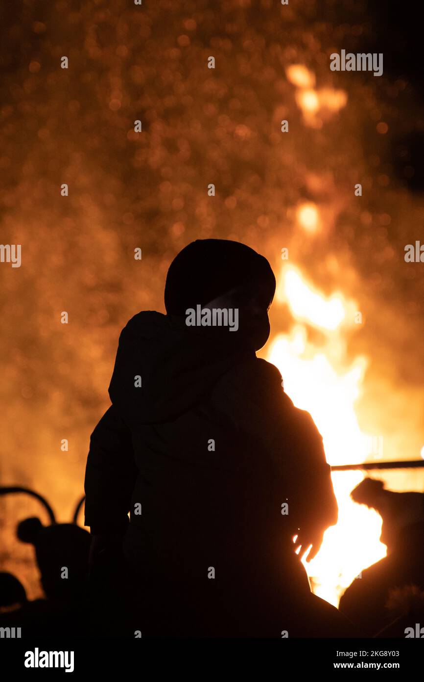 Children on their parents shoulders stood in front of a roaring bonfire ...
