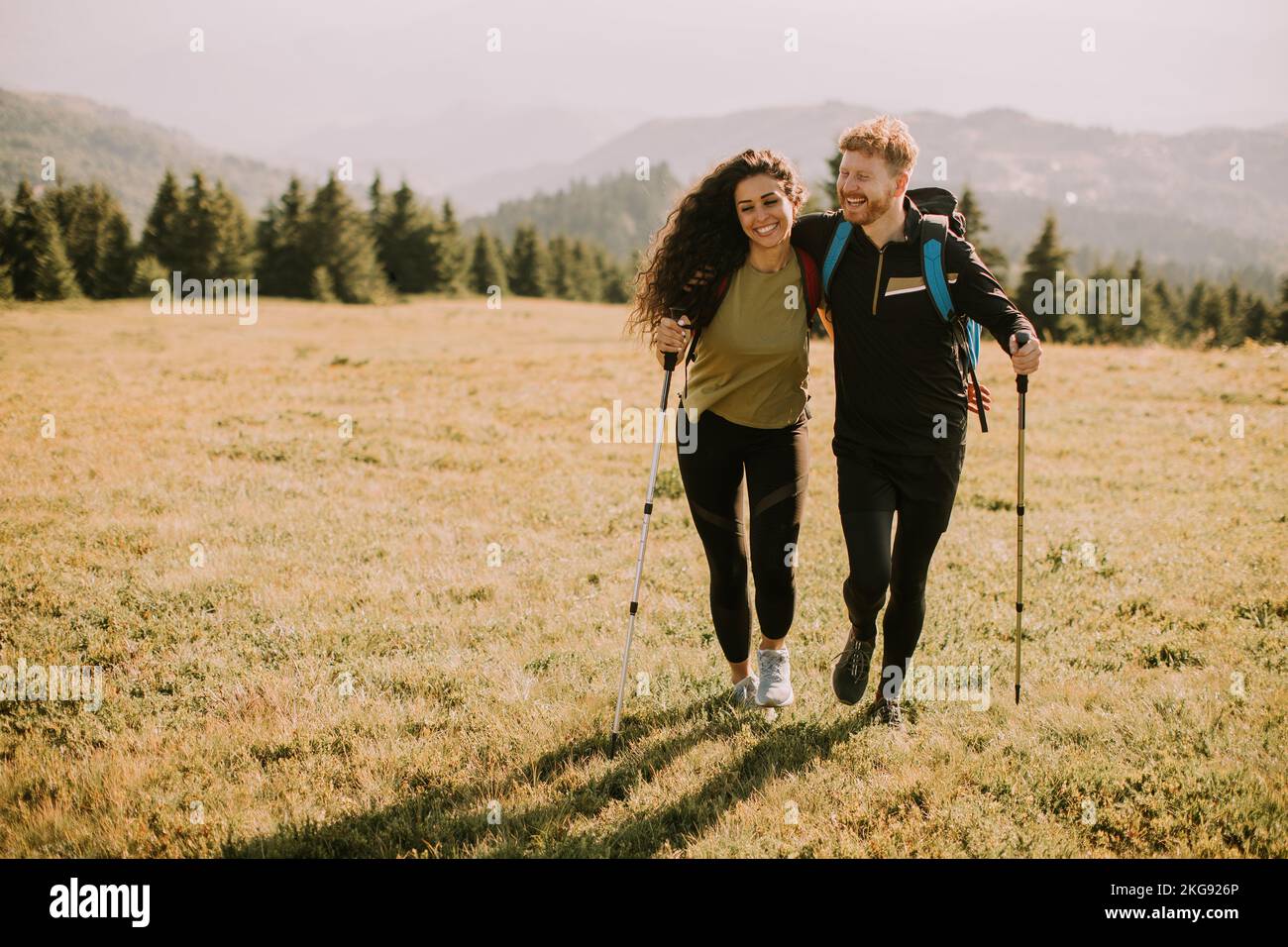 Smiling young couple walking with backpacks over green hills Stock ...