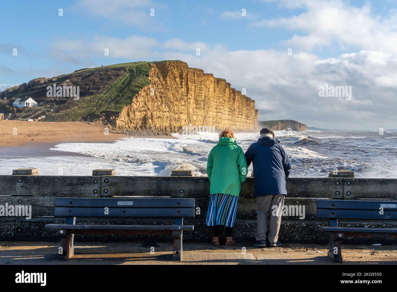 An elderly couple admire the view of the dramatic sunlit cliffs at West Bay, Dorset, UK Stock ...