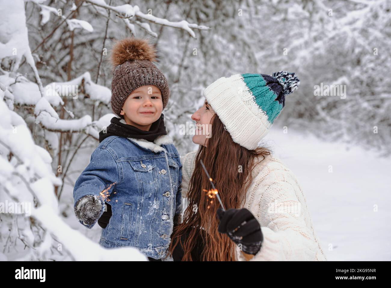 Mom and son are walking and light sparklers in the snow winter forest ...