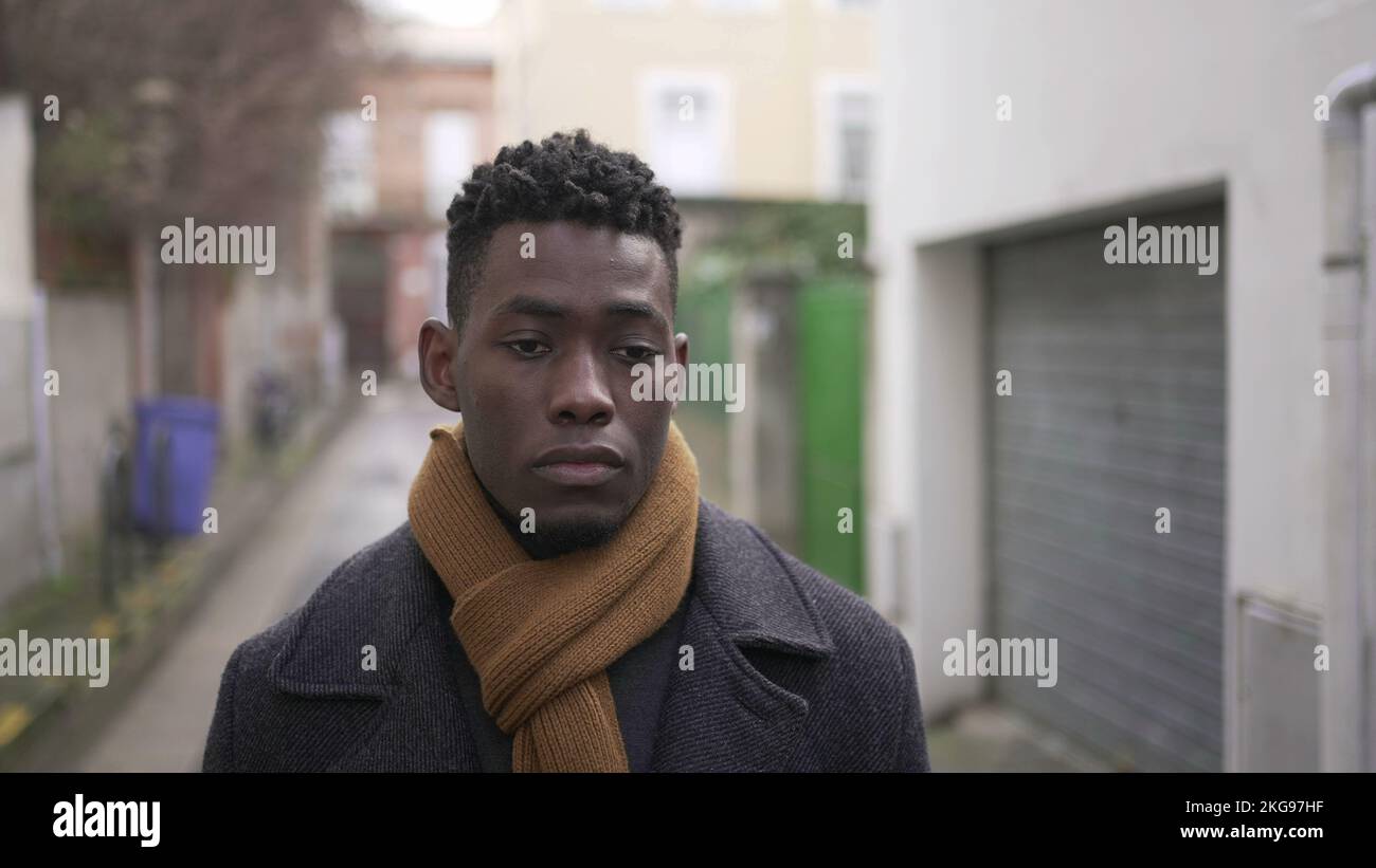 Sad upset black African man walking outside in city with moody ...
