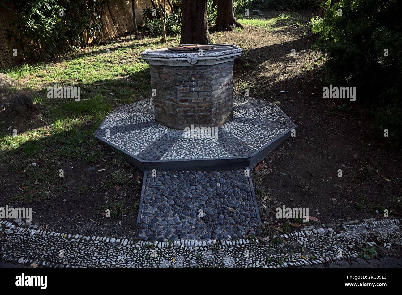 Old brick well next to a bush in a park Stock Photo - Alamy