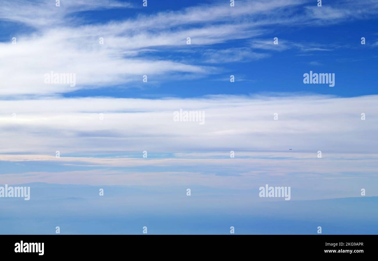 Vivid blue sky and white spreading clouds with an airplane flying in ...