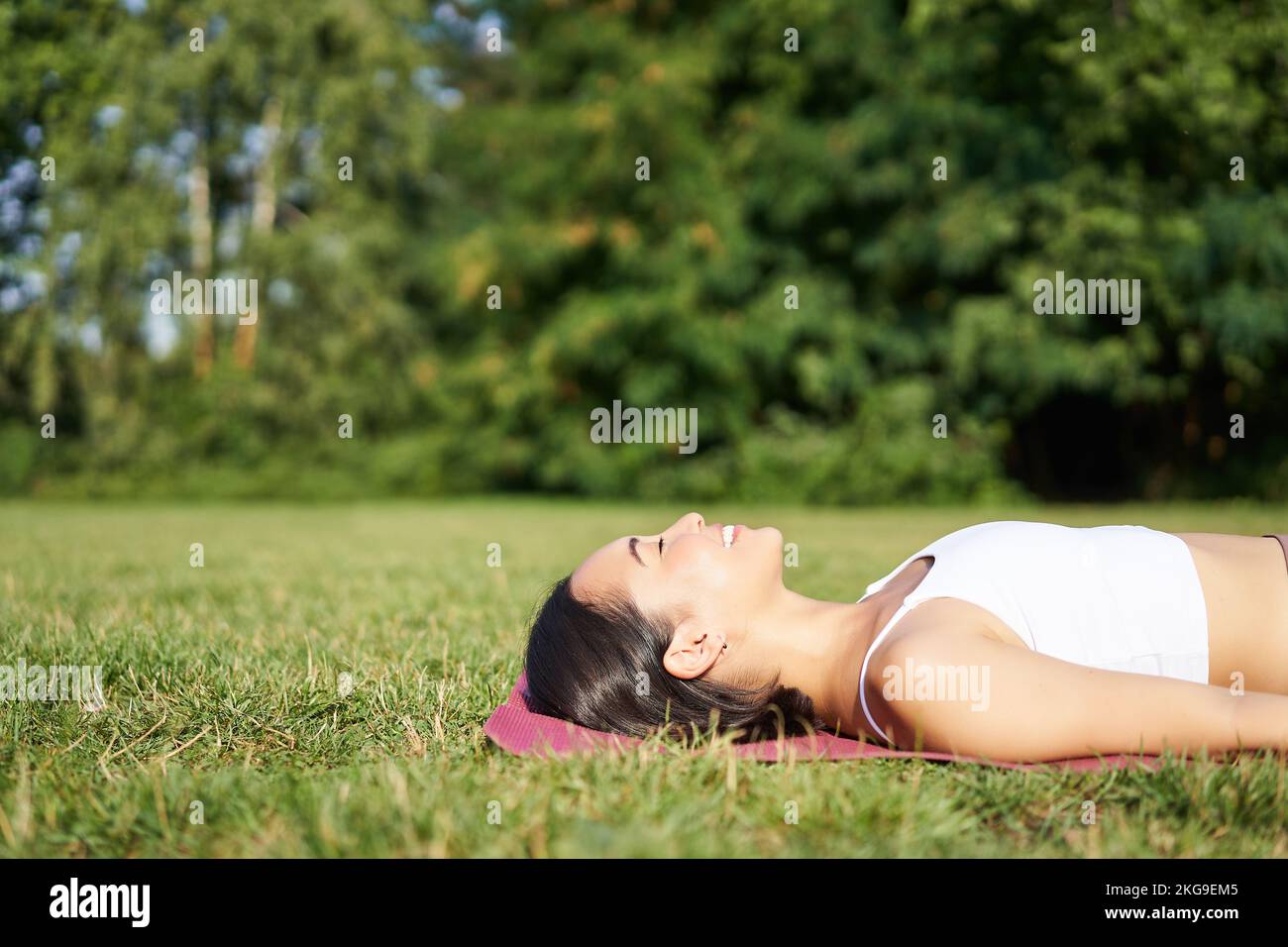 Young fitness girl lying on sport mat on lawn, breathing and meditating ...