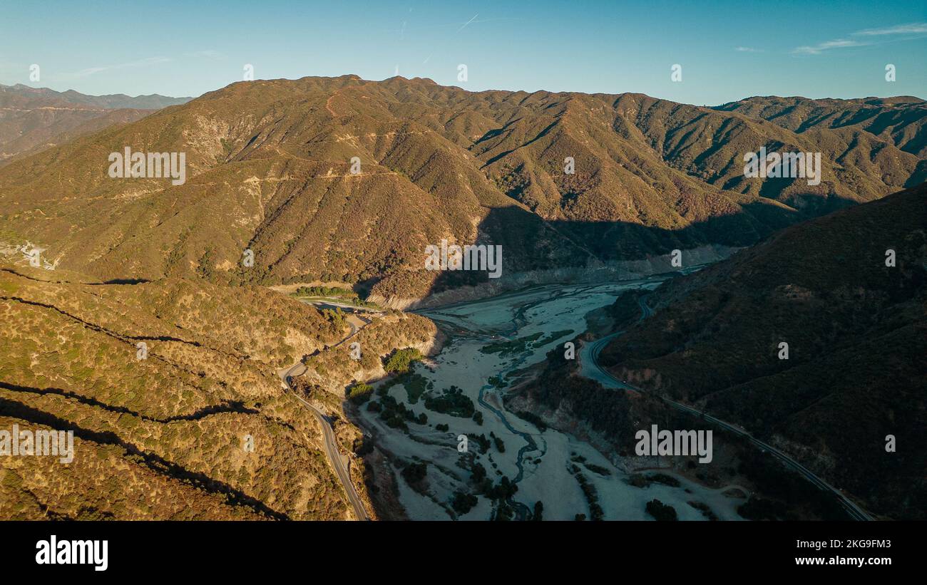 An aerial of a thin river flowing through the middle of green hills ...