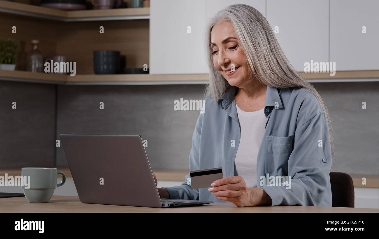 Happy old female caucasian consumer grey-haired granny shopper pay ...