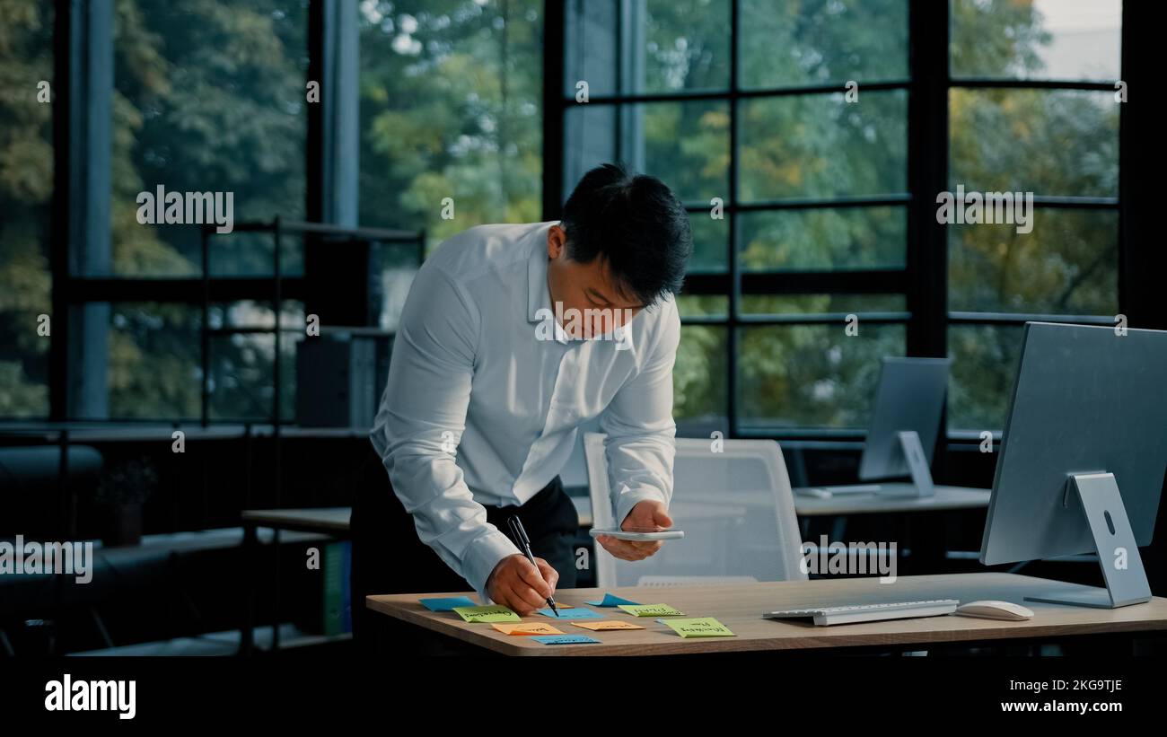 Korean asian employee businessman stand at desk in office write on memo stickers manage project ...