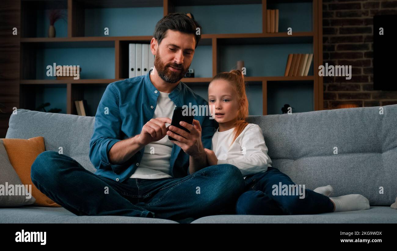 Happy family young child girl and single daddy look at modern gadget ...