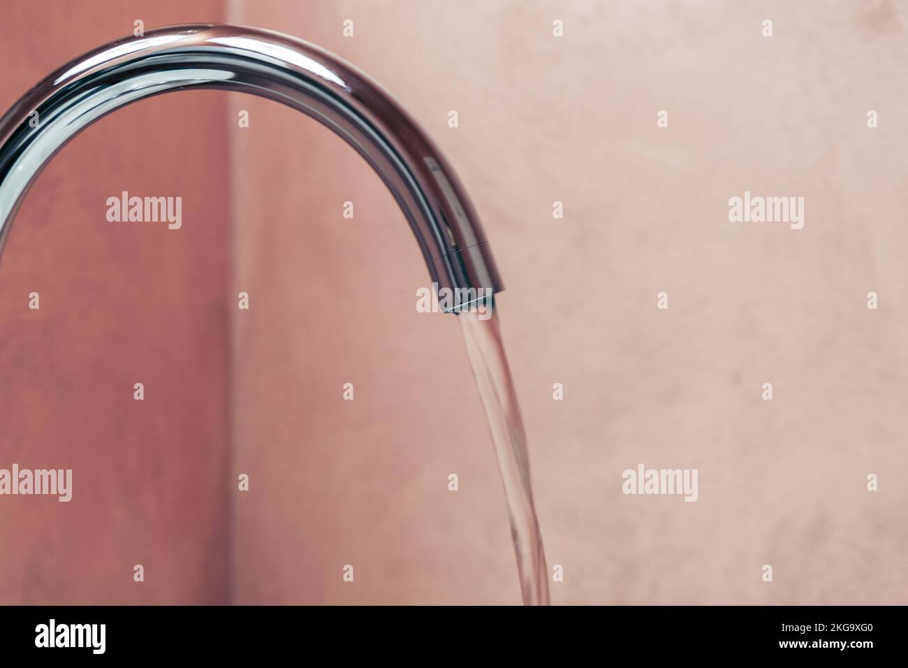 Water pours out of a shiny steel tap in a bathroom, close up photo ...