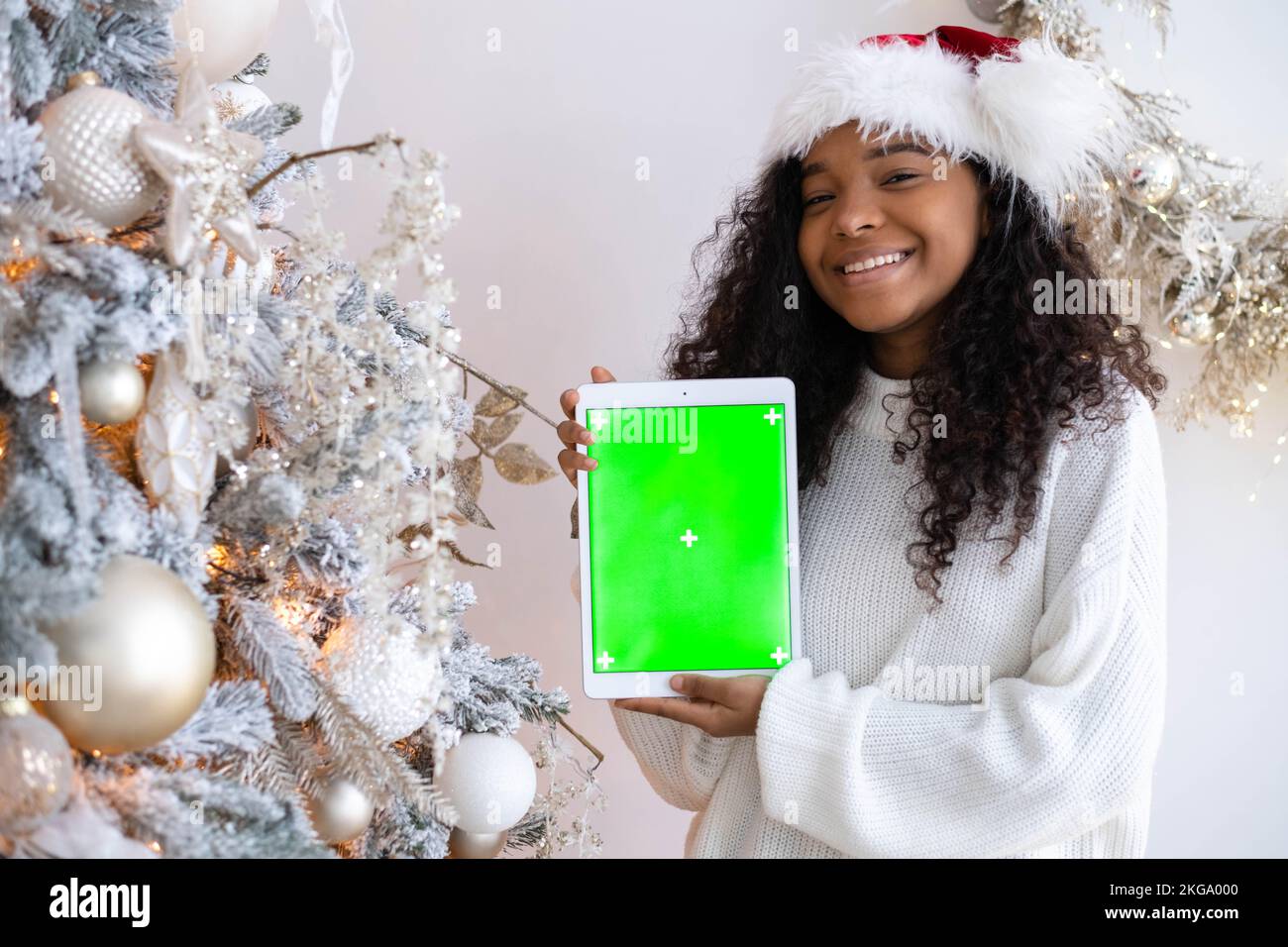 Smiling black girl in Santa hat showing tablet with green screen ...