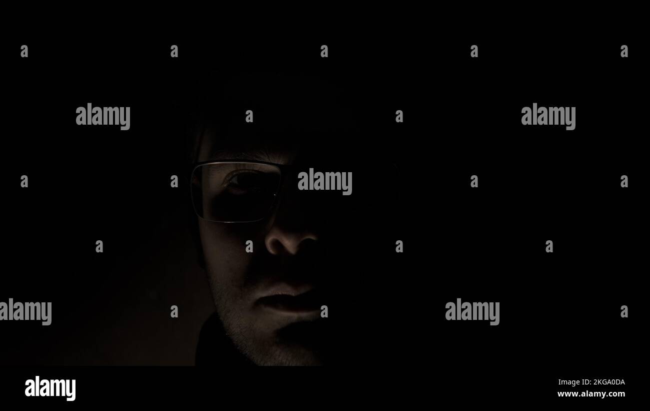the man in glasses looking in camera on a black background in low key ...