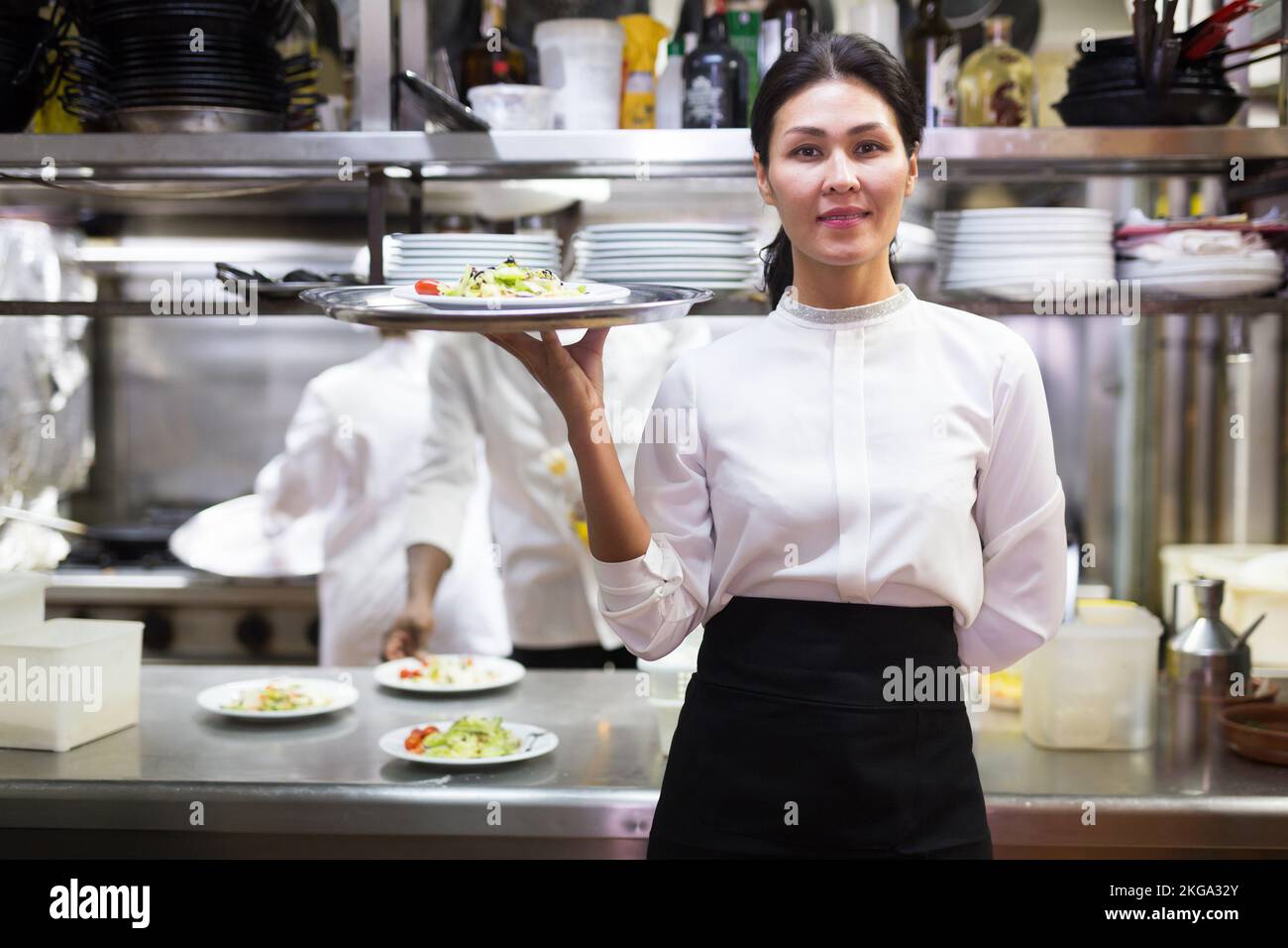 portrait of happy female waitress standing in white kitchen in cafe ...