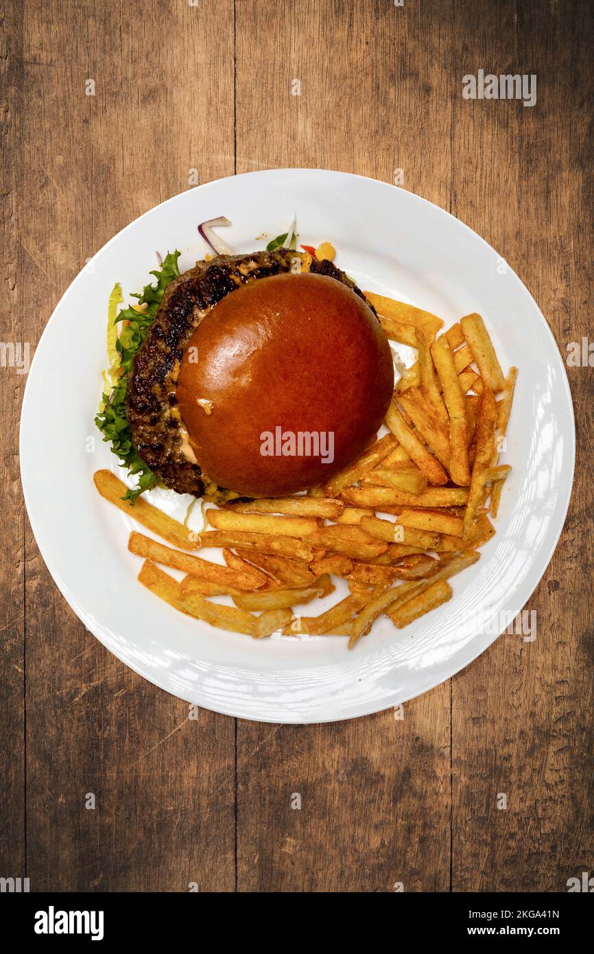 A vertical top view of a burger with fries on a white plate on a rustic ...
