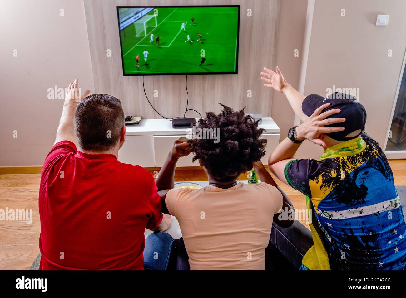 Back view of friends watching a football match on TV supporting their ...