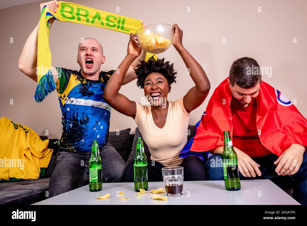 Friends watching a football match on TV, cheering for their national ...