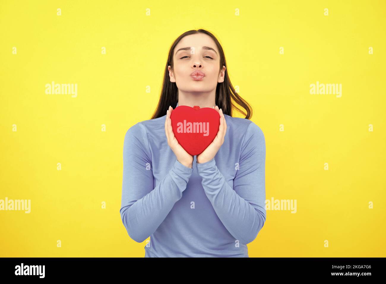 Beautiful girl holding valentines gift on yellow background. Portrait ...