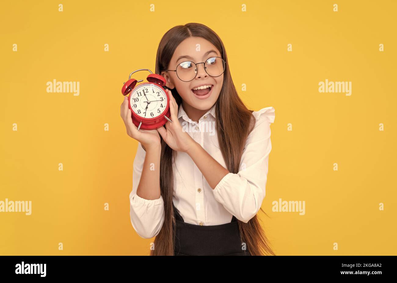 amazed teen girl in school uniform and glasses listen alarm clock ...