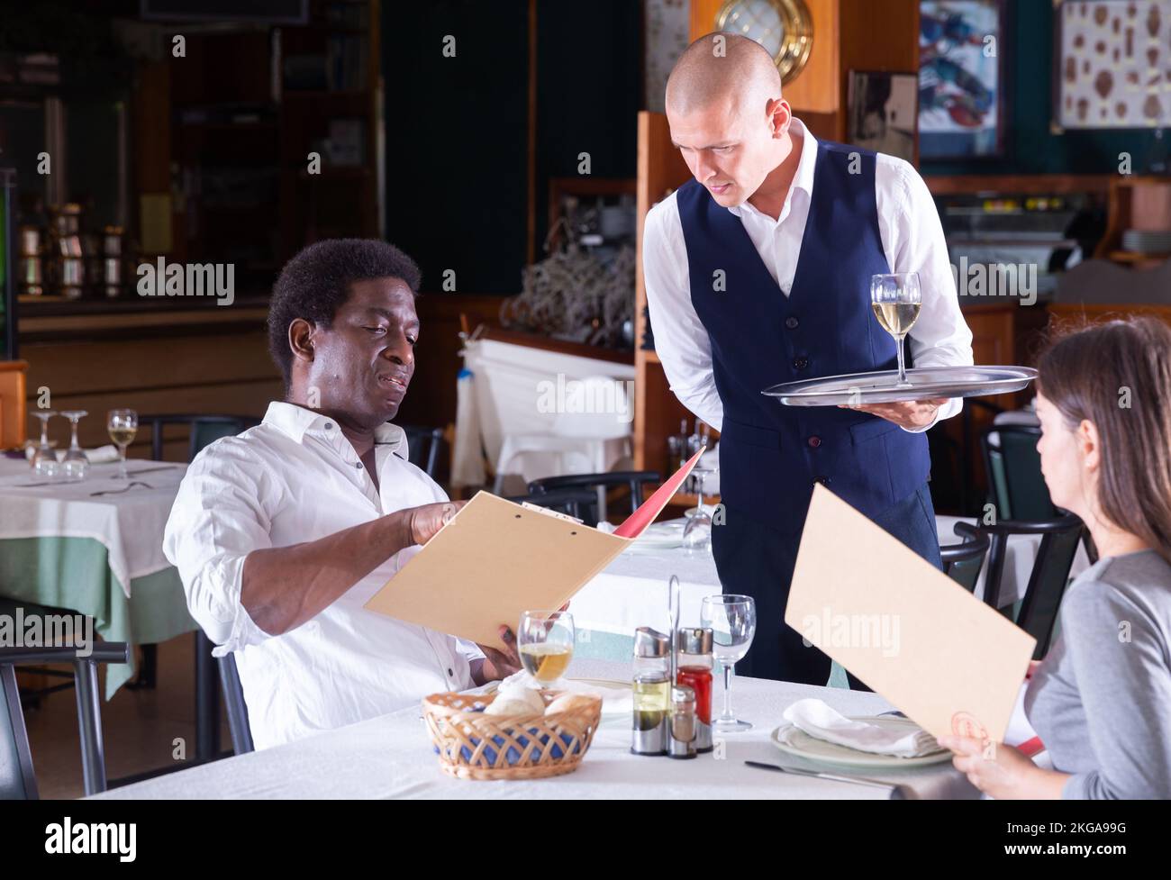Polite waiter helping guests in choosing meals from menu Stock Photo ...
