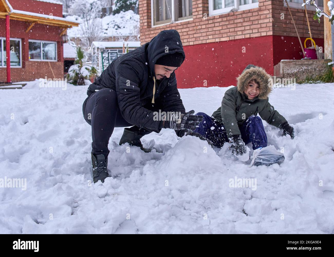 Latino father and son squatting playing in the snow one winter ...