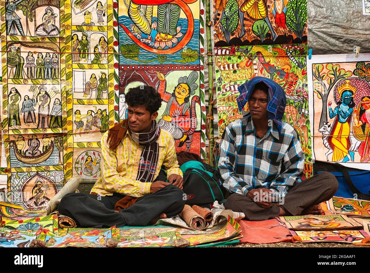Two Indian men sitting surrounded by paintings in the Poush Mela ...