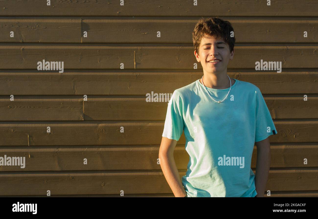 A young happy Hispanic boy with a blue shirt posing near a wooden wall ...