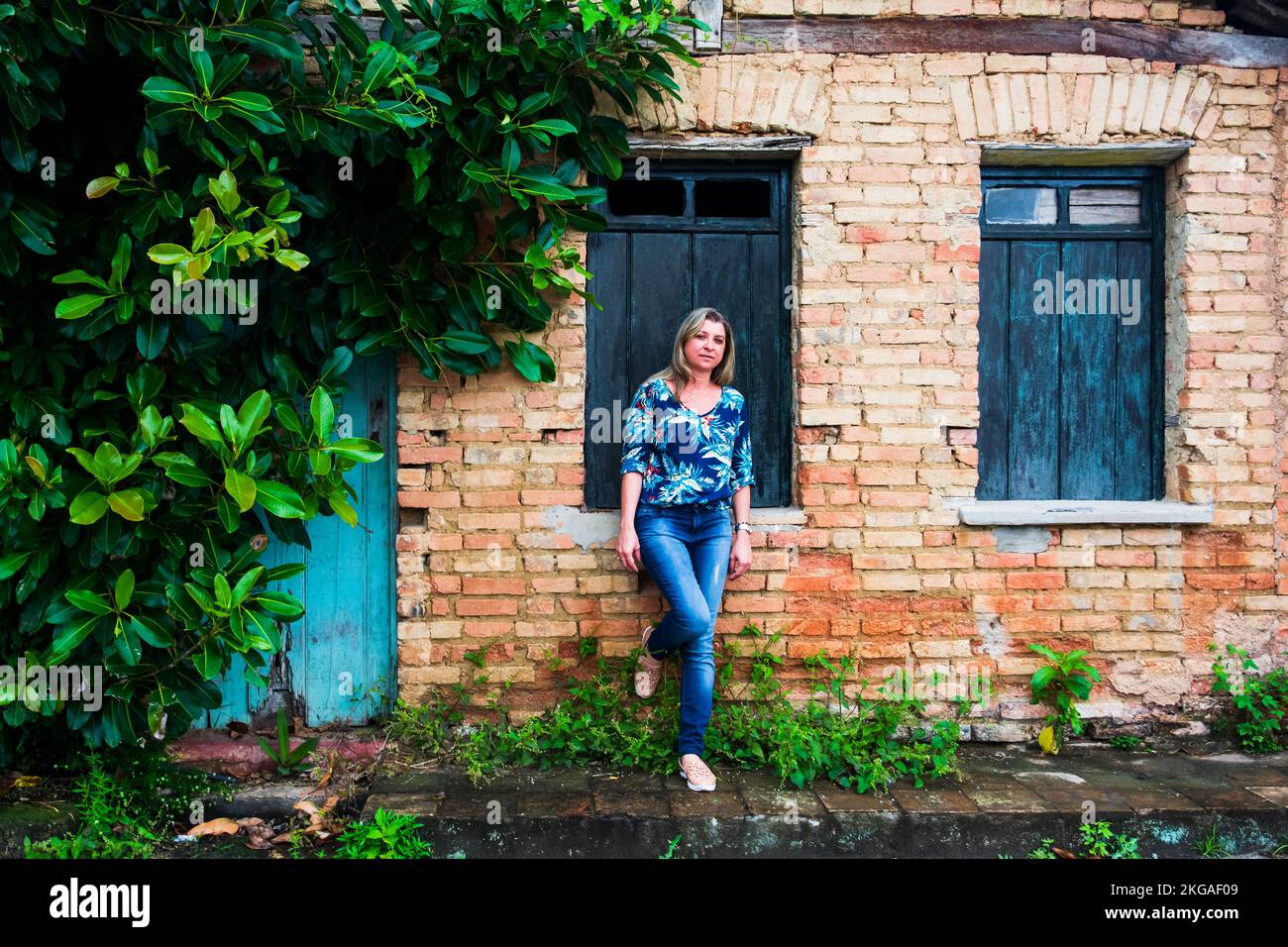 Woman leaning against a window of an old house. Brick facade and leaves ...