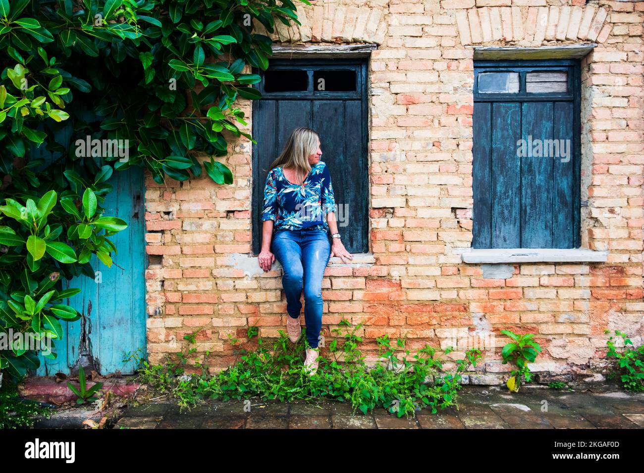 Woman leaning against a window of an old house. Brick facade and leaves ...