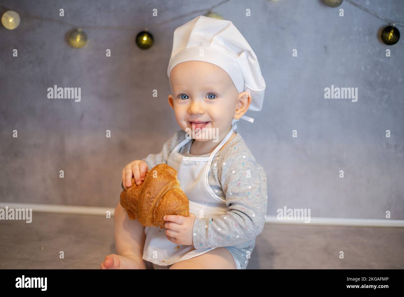 a cute little girl in a chefs hat and an apron sits at home on the ...