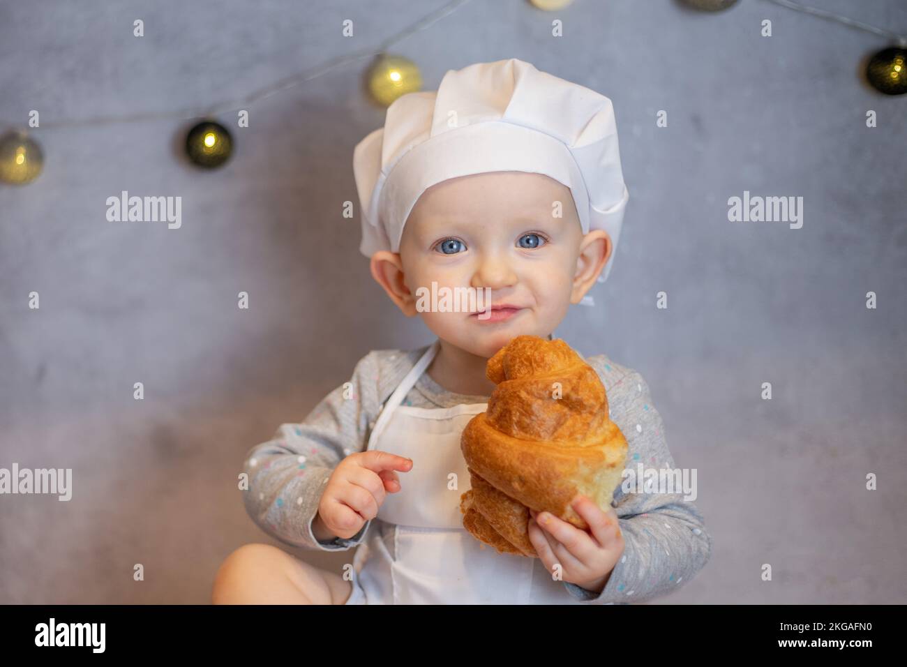 a cute little girl in a chefs hat and an apron sits at home on the ...