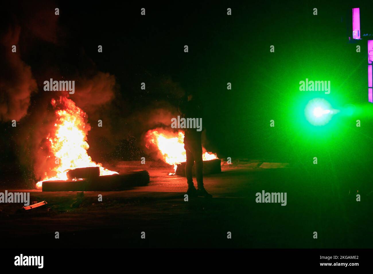 A laser beam is seen as demonstrators burn tires and close off the road ...