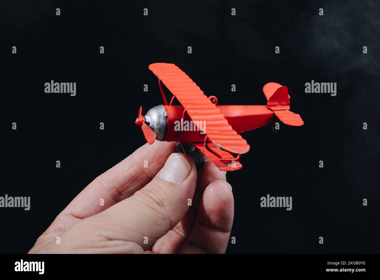 Hand holding a red toy plane on a black background Stock Photo - Alamy