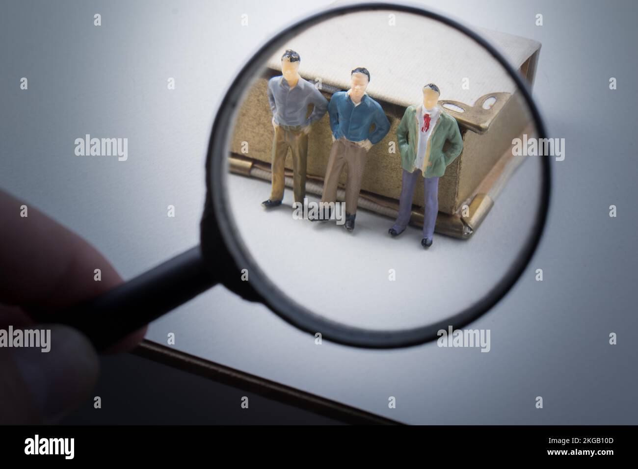 Tiny of men beside a book under magnifying glass Stock Photo - Alamy