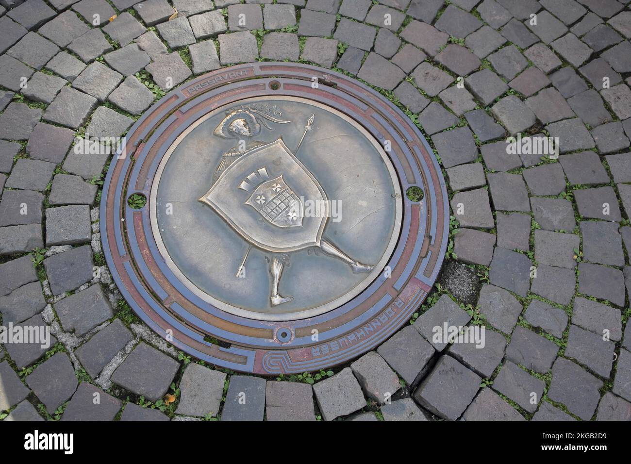 Round manhole cover with city coat of arms and paving stones, ground ...